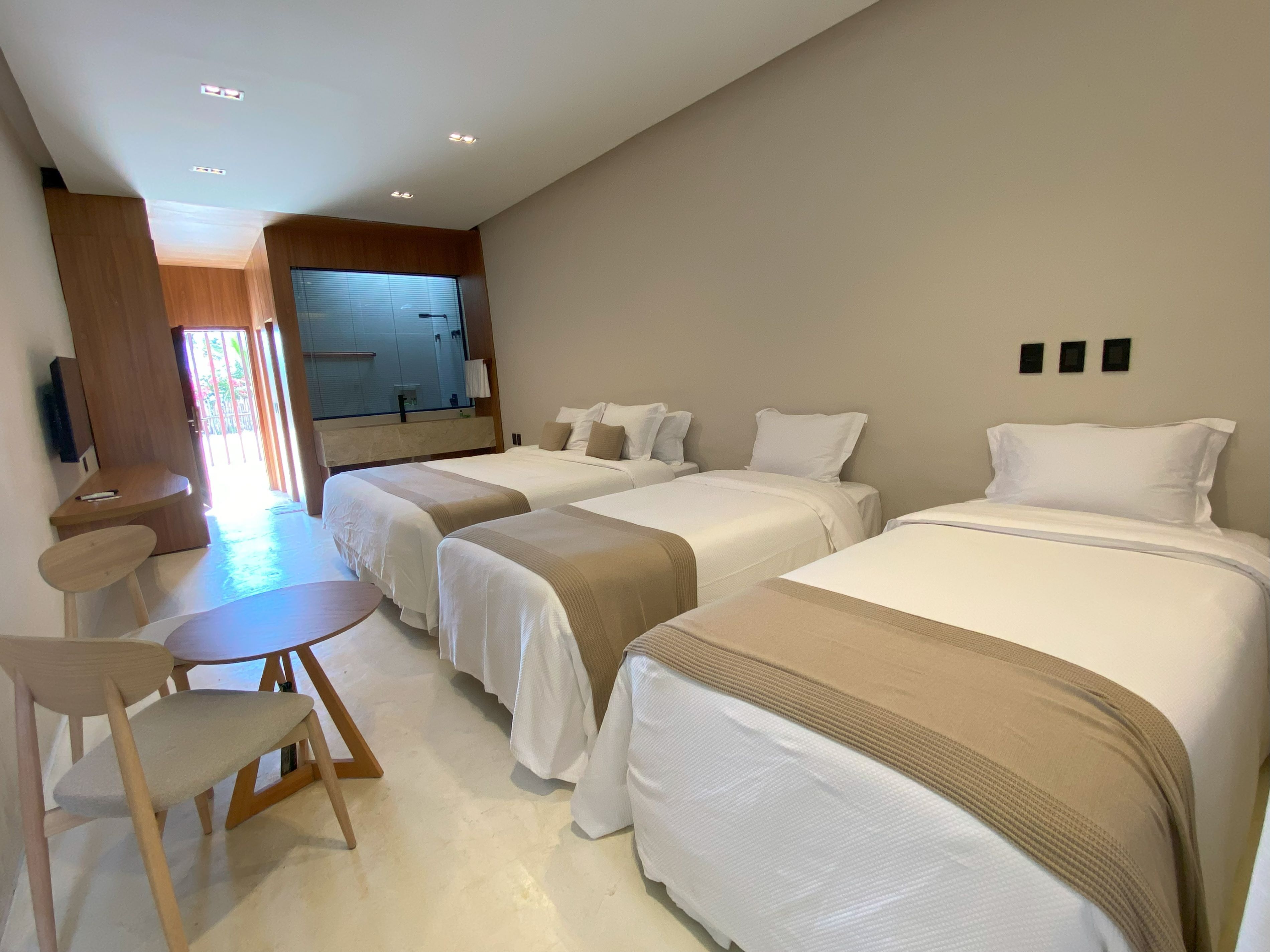 Quarto de hotel com duas camas, uma mesinha, uma cadeira e uma televisão.