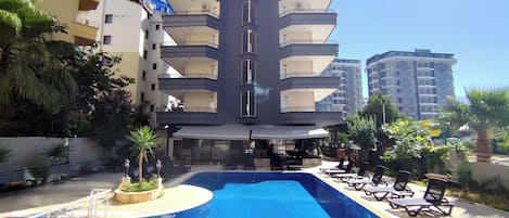Um hotel moderno com piscina central, várias varandas e céu limpo.