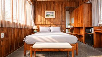 Quarto com painéis de madeira, uma cama, mesa de cabeceira, abajur e micro-ondas.