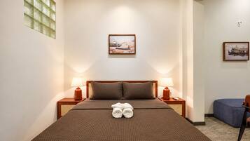 Quarto de hotel com uma cama grande, duas luminárias de cabeceira, um quadro na parede e uma pequena área de estar com uma poltrona.