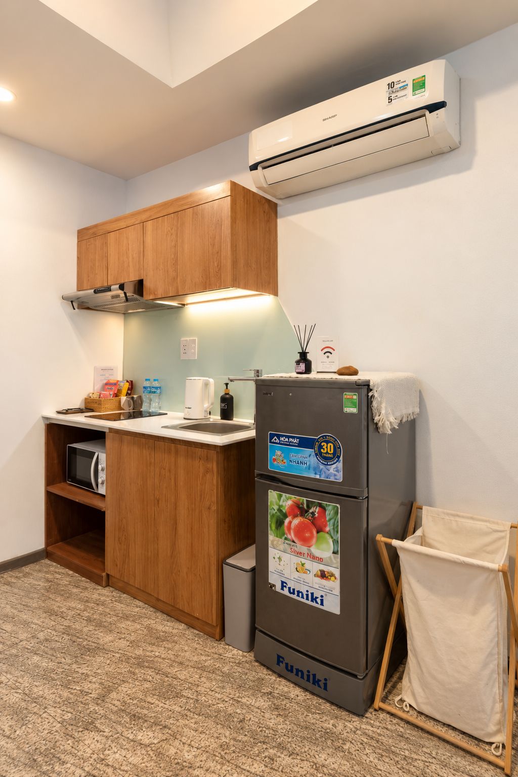 Uma cozinha compacta com armários de madeira, micro-ondas embutido, geladeira com adesivo promocional e ar-condicionado fixado na parede.