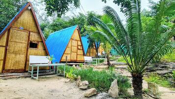 Uma fileira de cabanas com telhados de palha e detalhes azuis, cercada por vegetação e pedras.