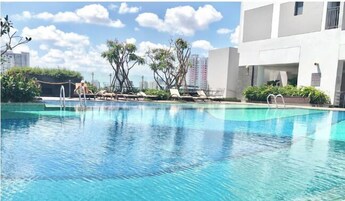 Piscina com espreguiçadeiras e palmeiras, cercada por edifícios modernos.
