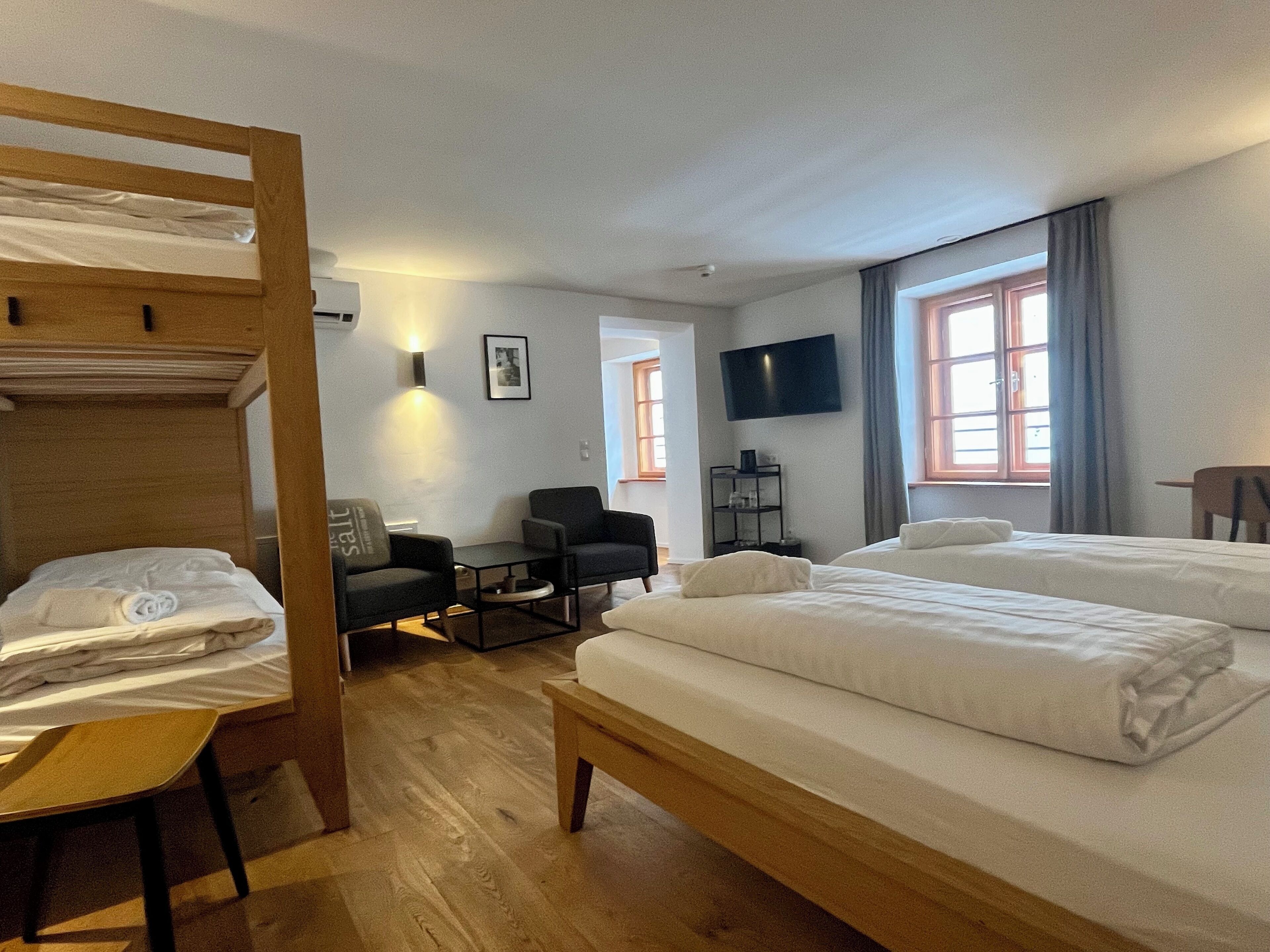 Quarto de hotel com duas camas, uma escrivaninha, uma cadeira, uma televisão e uma janela.