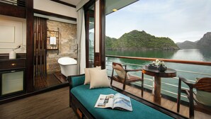 Uma varanda com vista para um lago e colinas, um sofá, uma mesa com um livro e um banheiro com banheira.
