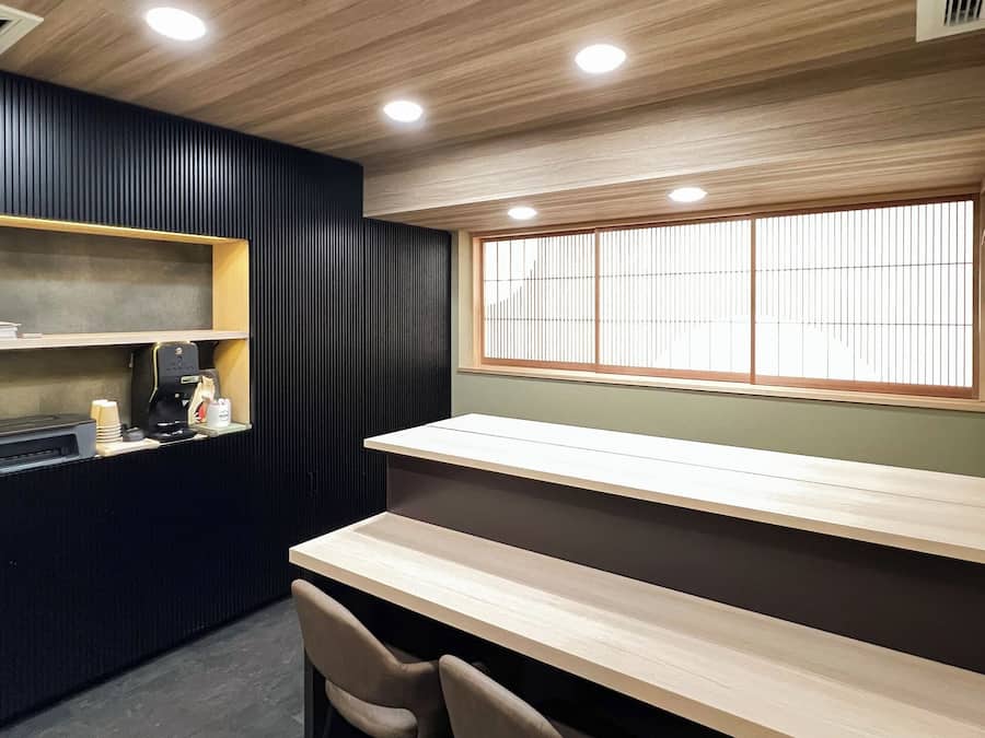 Um espaço de escritório moderno com uma parede escura, prateleiras de madeira, uma janela com persianas e uma mesa com cadeiras.