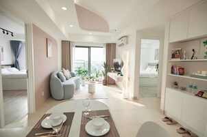 Quarto de hotel moderno com área de refeições, sofá, varanda com plantas e minibar.