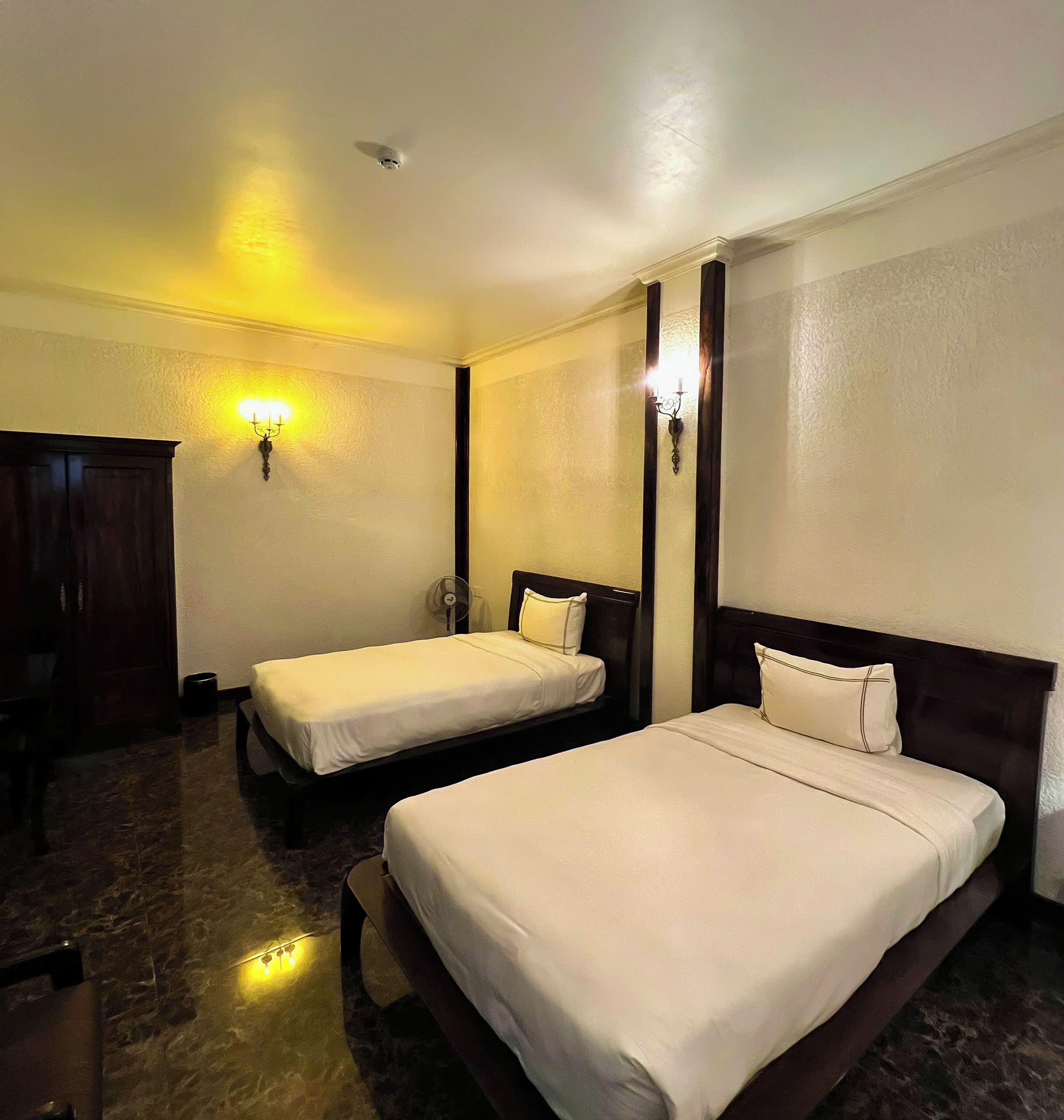 Quarto de hotel com duas camas, um guarda-roupa de madeira e um espelho.