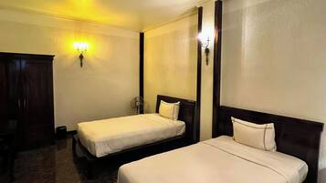 Quarto de hotel com duas camas, um guarda-roupa de madeira e um espelho.