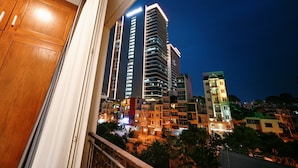 Vista noturna de um horizonte urbano com edifícios altos, uma varanda e a rua lá embaixo.