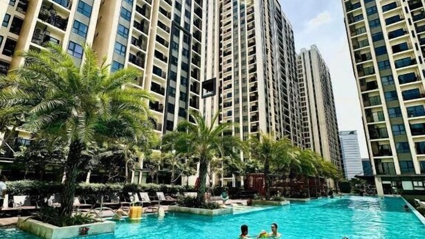 Piscina rodeada por edifícios residenciais altos, palmeiras e cadeiras de lounge.
