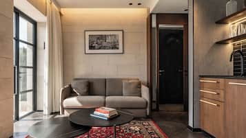Uma sala de estar moderna com um sofá, uma mesa de centro e um tapete. Há um quadro na parede e uma área de cozinha com armários de madeira.