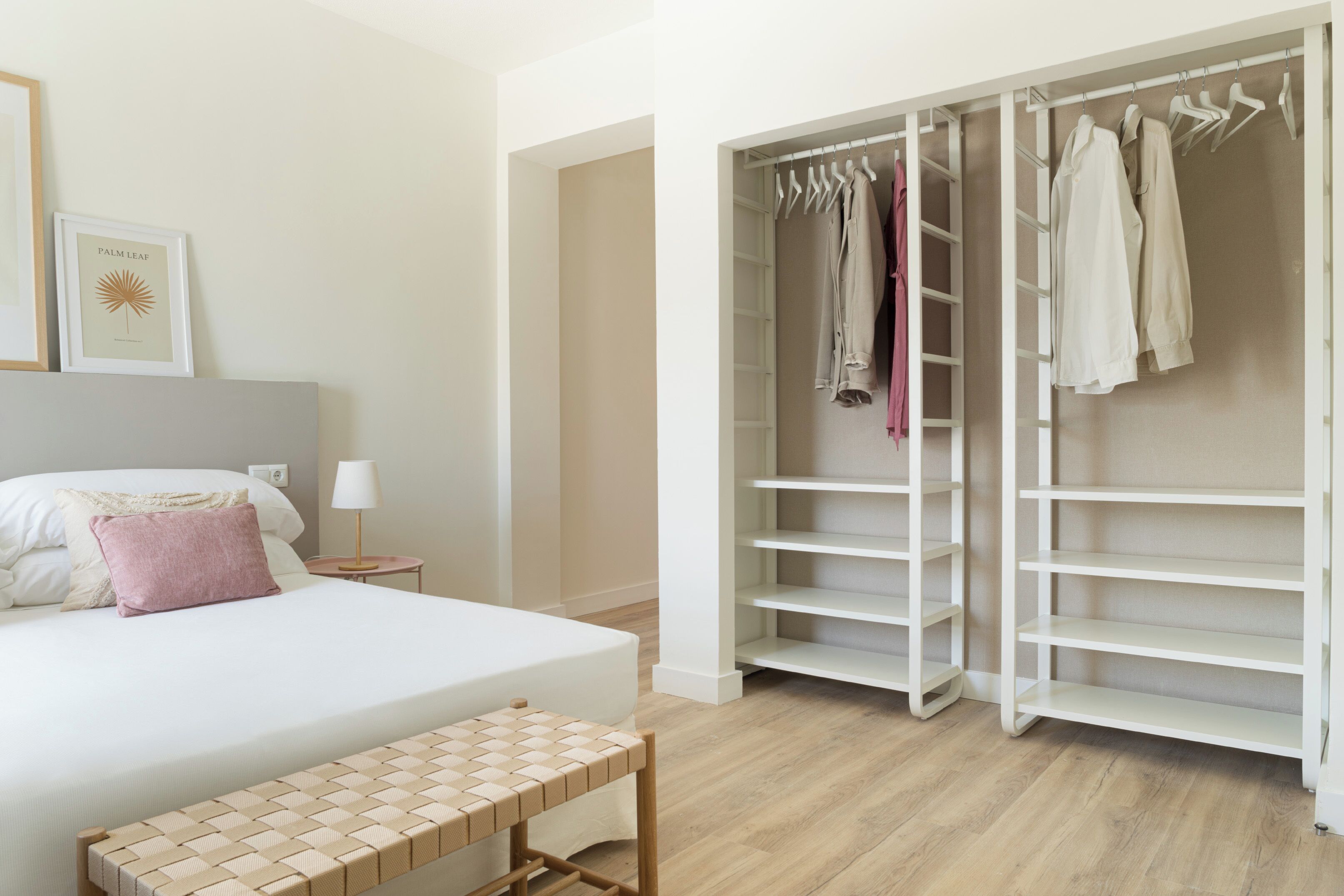 Quarto com cama, mesa de cabeceira, banco e um closet espaçoso com prateleiras e cabides.