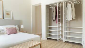 Quarto com cama, mesa de cabeceira, banco e um closet espaçoso com prateleiras e cabides.