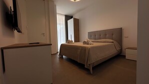 Quarto com cama, mesa de cabeceira, guarda-roupa e televisão na parede.