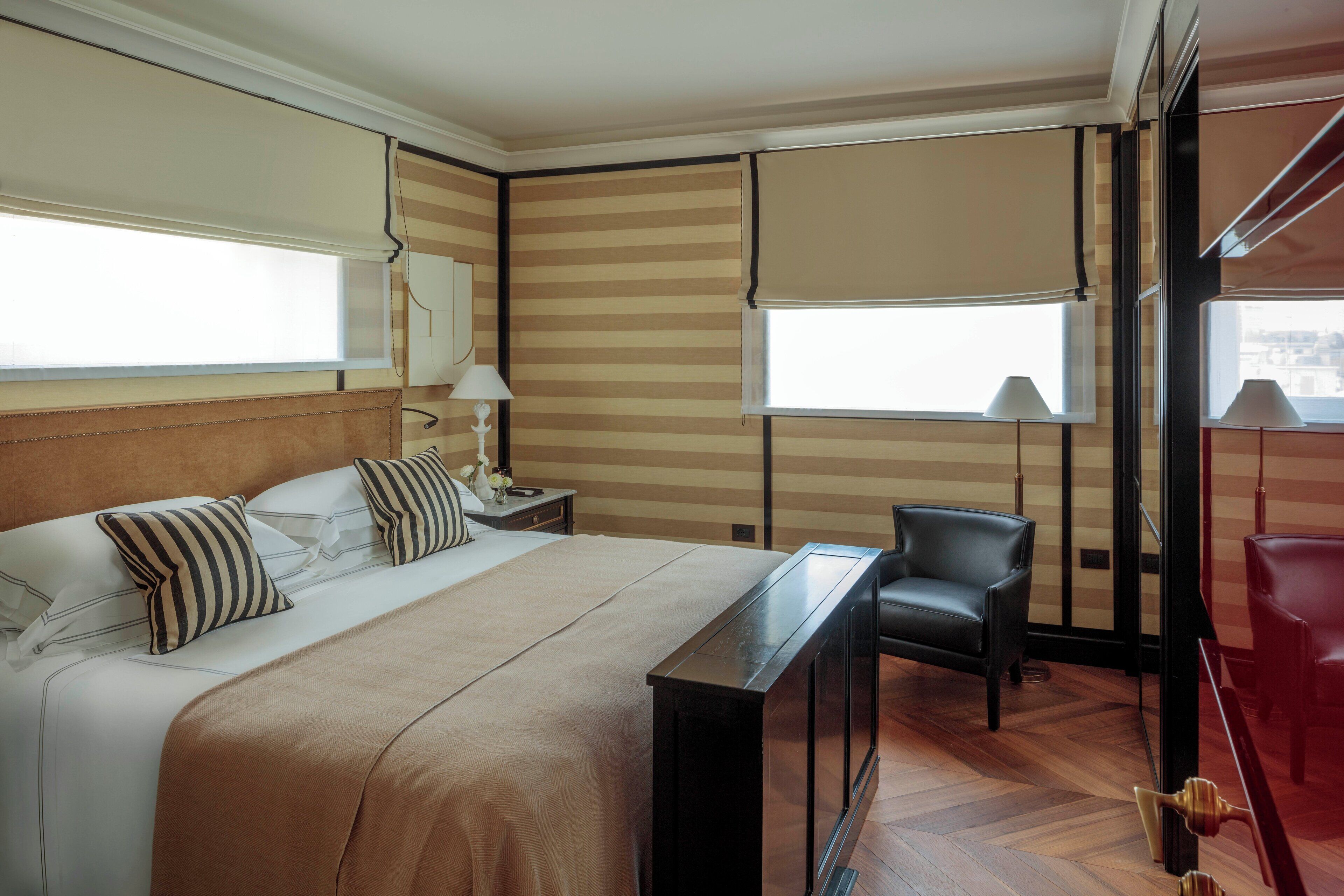 Quarto de hotel com uma cama grande, uma escrivaninha, uma cadeira e uma janela com persianas.