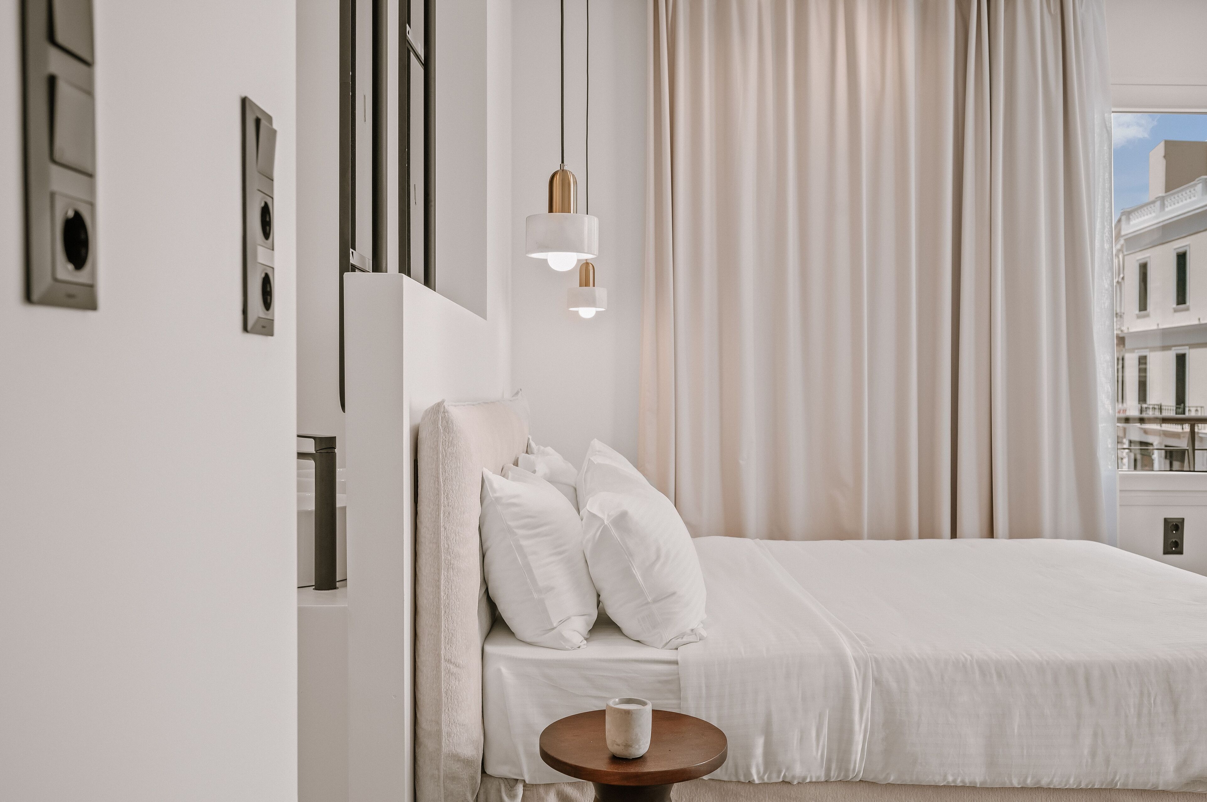 Quarto de hotel moderno com uma cama grande, uma mesa redonda e vista para edifícios pela janela.