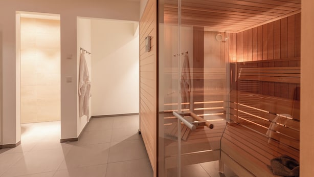 Uma área de spa moderna com painéis de madeira, uma sauna envidraçada e um banco com toalhas.