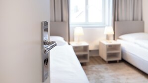 Quarto de hotel com cama, mesa de cabeceira, luminária e janela com cortinas.