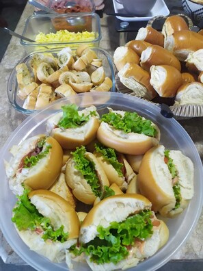 Buffet com diversos alimentos, incluindo pães, ovos mexidos e fatias de pão.