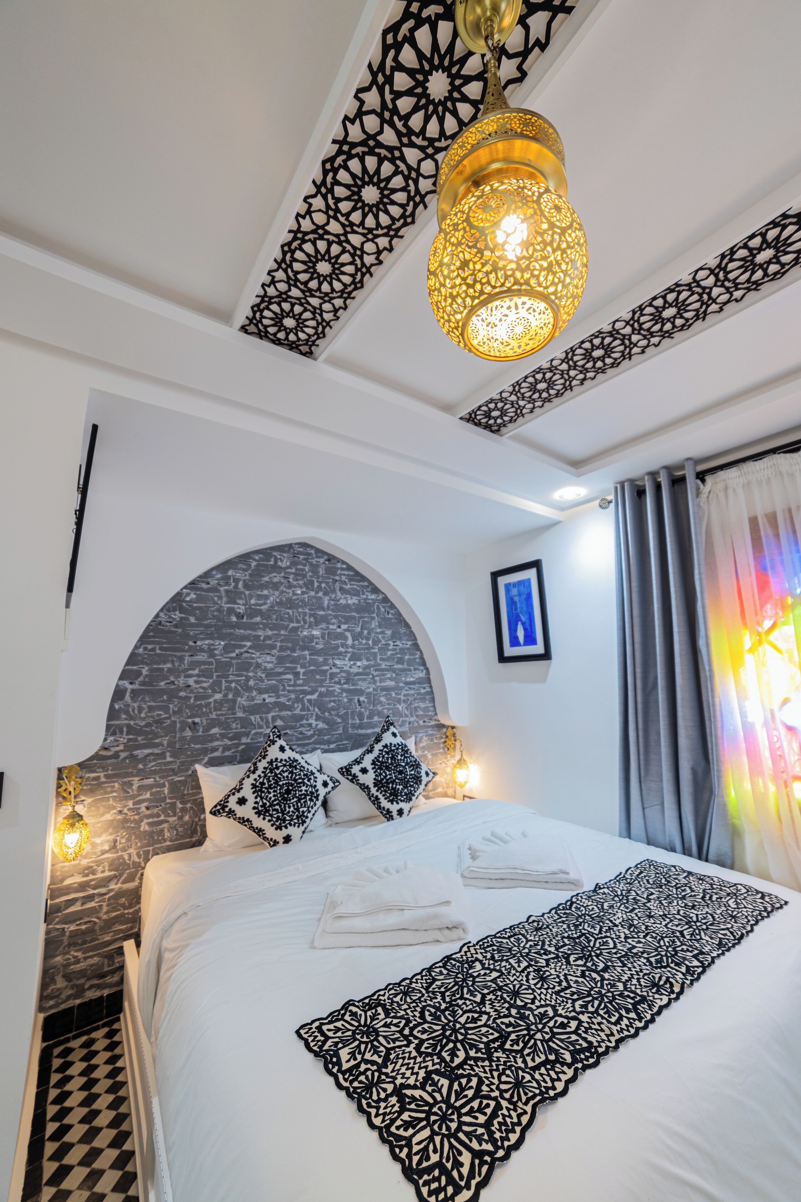 Quarto de hotel com cama, teto decorativo e luminária fixa na parede.