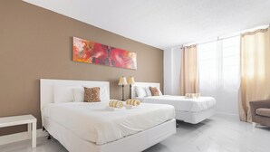 Quarto de hotel com duas camas, um banco, um quadro e uma janela com cortinas.