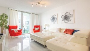 Uma sala de estar moderna com um sofá branco, poltronas vermelhas e uma grande janela com cortinas.
