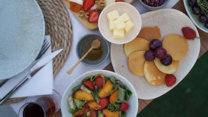 Um buffet de café da manhã com diversos queijos, frutas, panquecas e uma salada.