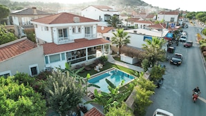 Uma área residencial com uma piscina grande, uma rua com carros estacionados e casas com telhados de telha vermelha.