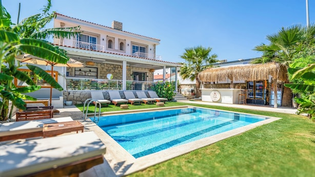 Uma área de piscina com espreguiçadeiras, um bar e um prédio de pedra com varanda.