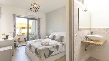 Quarto de hotel moderno com cama, escrivaninha, cadeira, vista para a varanda e banheiro com pia e espelho.