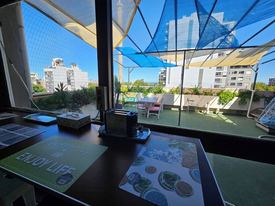 Quarto com vista para um jardim no terraço, uma mesa com jogo americano e uma torradeira no parapeito da janela.