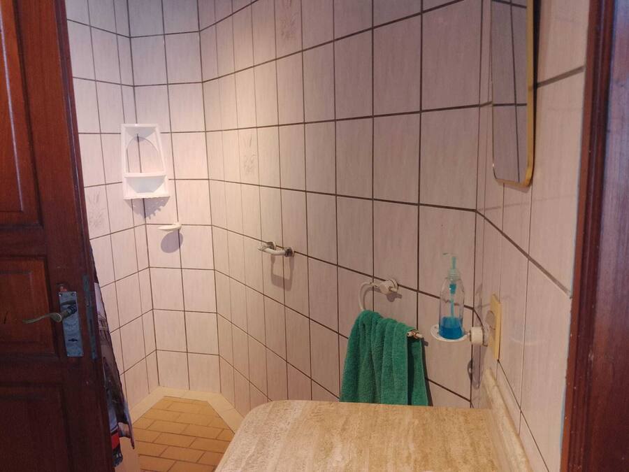 Um banheiro pequeno com chuveiro, vaso sanitário e pia. Há uma toalha verde pendurada na parede.