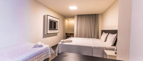 Quarto de hotel com duas camas, uma escrivaninha, uma televisão e ar condicionado.