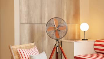 Um quarto com uma cadeira de vime, um ventilador tripé e uma almofada listrada.
