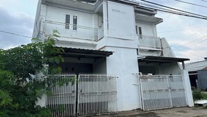 Um edifício de dois andares com fachada branca, varanda no andar superior e entrada protegida por portão.