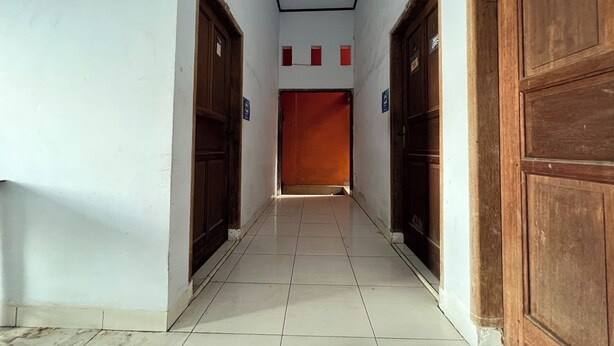 Um corredor com portas de madeira, soalho em azulejos e uma porta vermelha ao fundo.