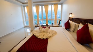 Quarto de hotel com uma cama grande, vista das montanhas pelas janelas e cabeceira de madeira.