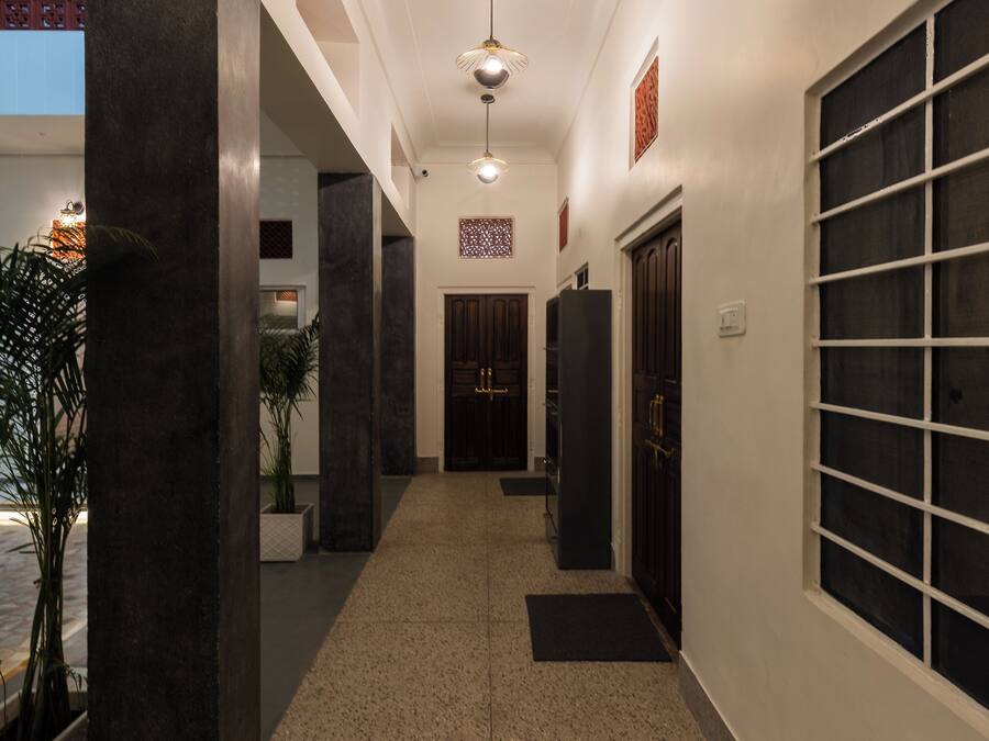 Um corredor com piso de azulejos, pilares escuros e uma porta no final.