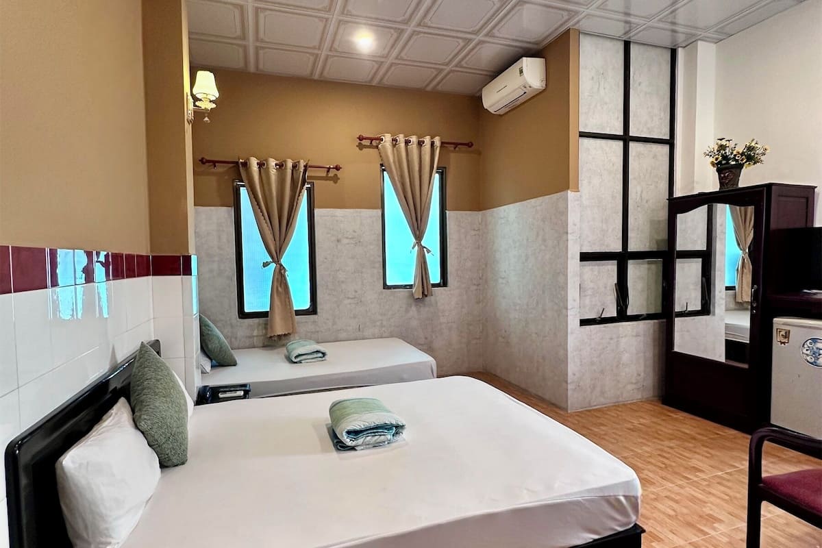 Quarto de hotel com duas camas, piso de madeira, teto com iluminação embutida e ar condicionado.