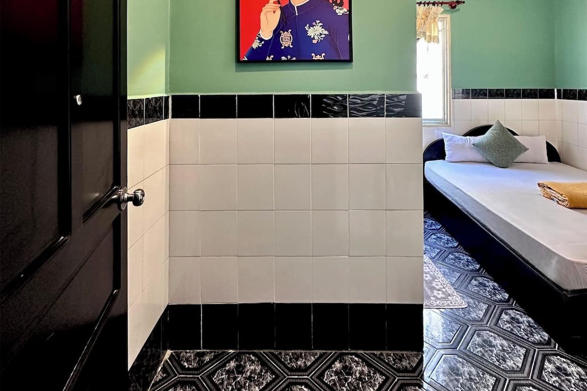 Quarto de hotel com uma cama, banheiro com parede azulejada e um quadro na parede.