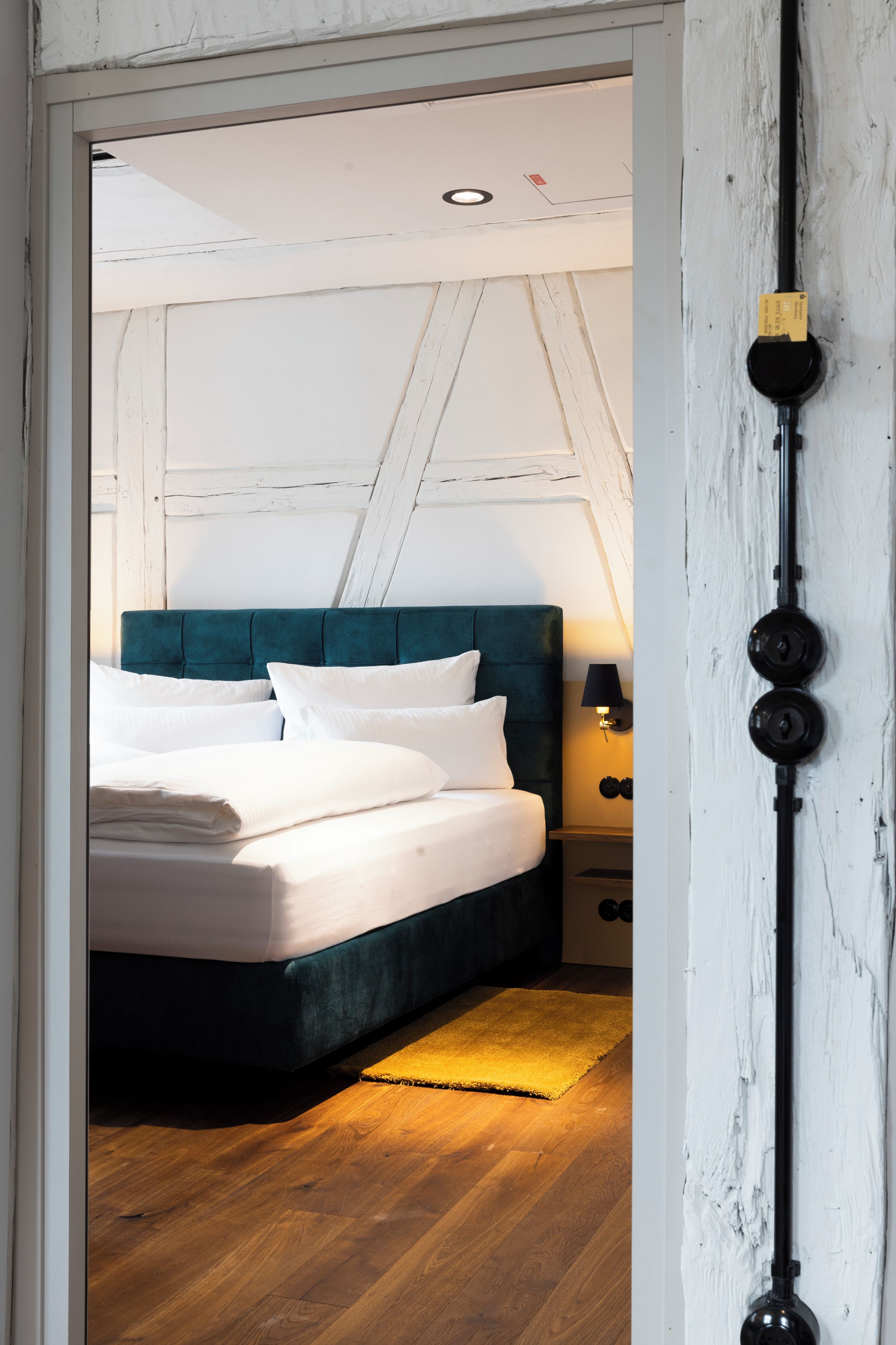 Quarto com cabeceira estofada em tom verde-água, roupa de cama branca e piso de madeira.