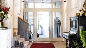 Um corredor com carpete vermelho, um piano de cauda e uma escadaria que leva a uma porta de vidro.