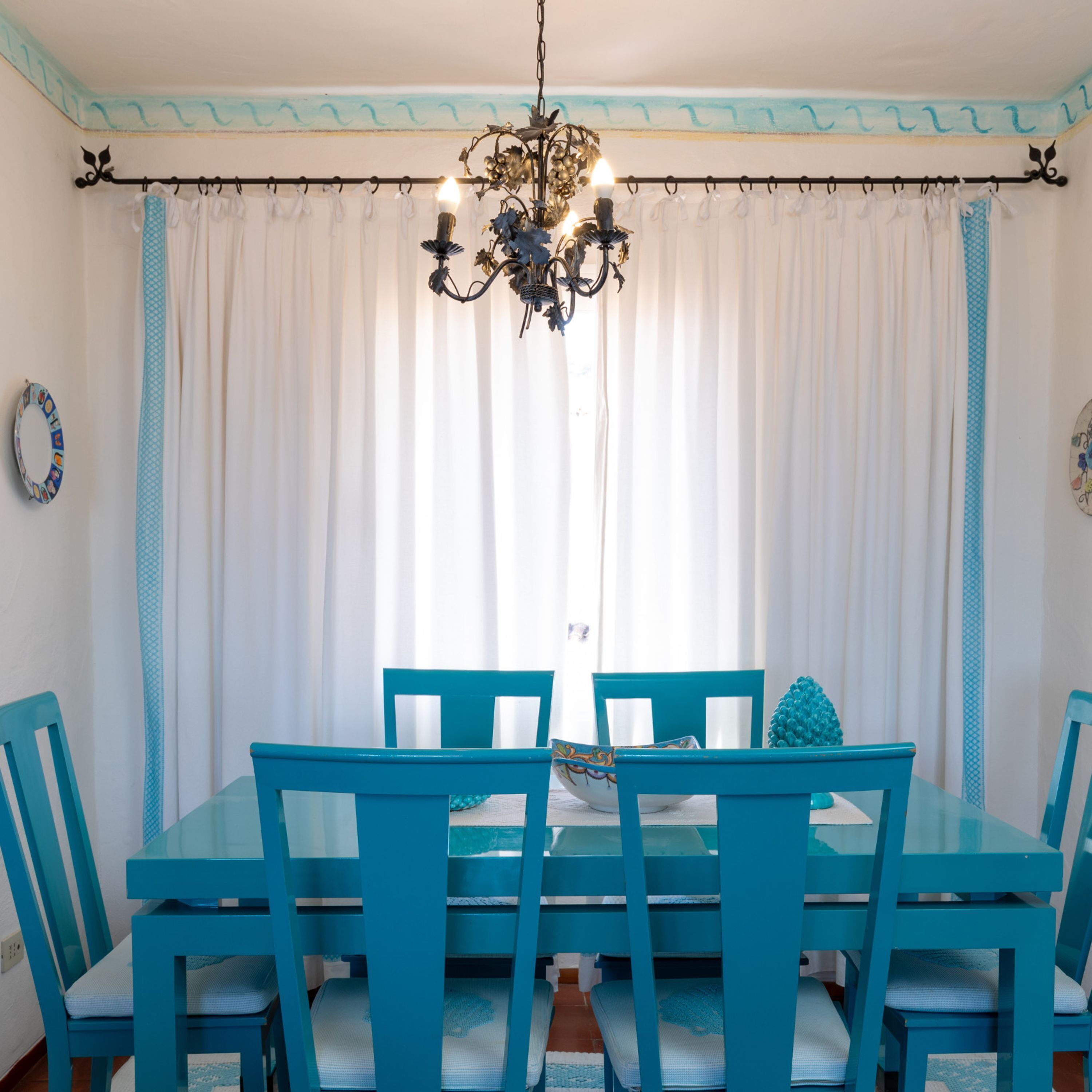 Uma sala de jantar com mesa, cadeiras, um lustre e cortinas.