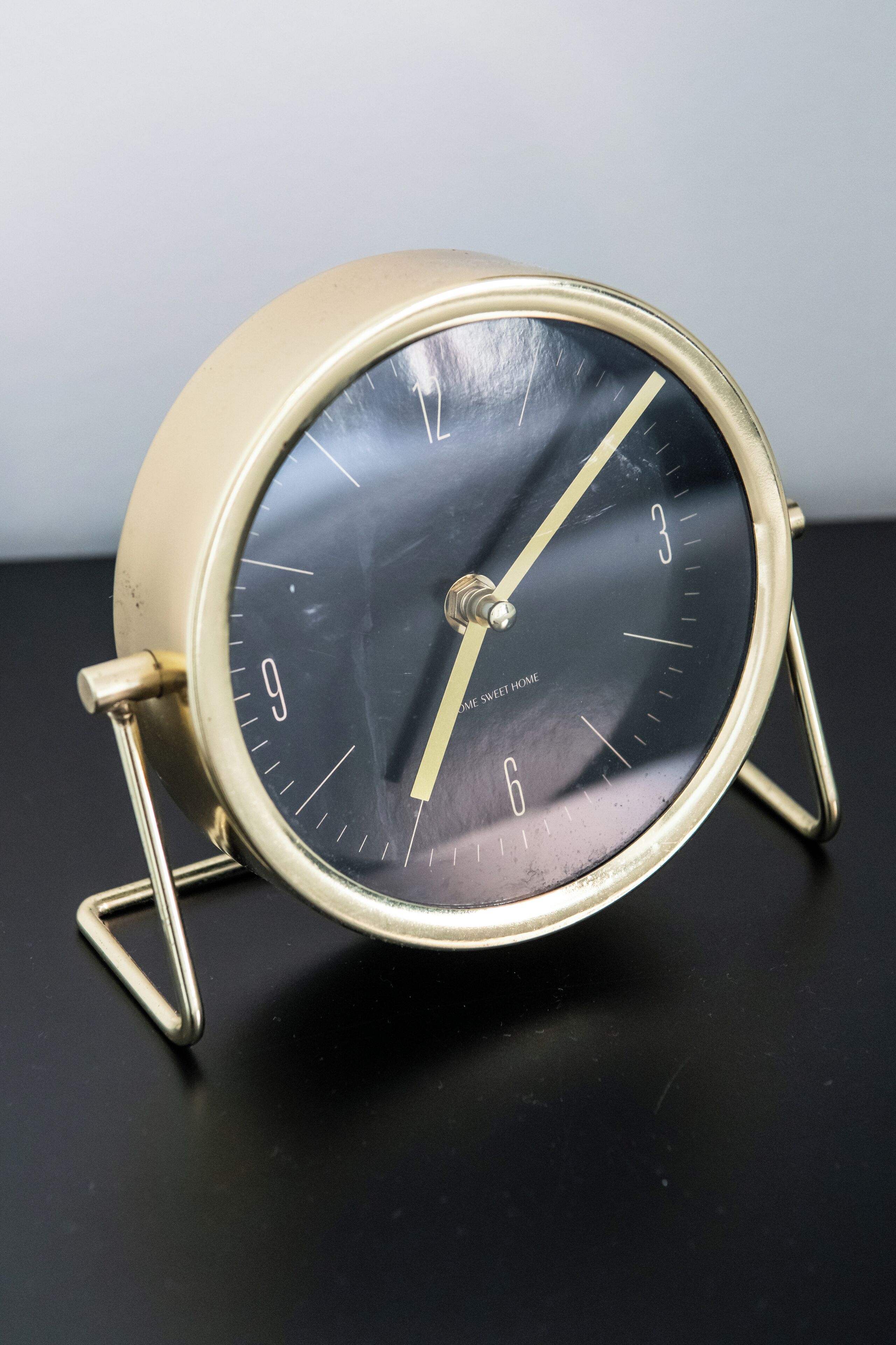 Um relógio despertador de estilo vintage com mostrador preto e detalhes dourados, posicionado sobre um suporte.