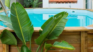 Uma área de madeira à beira da piscina, com uma piscina e grandes folhas verdes.