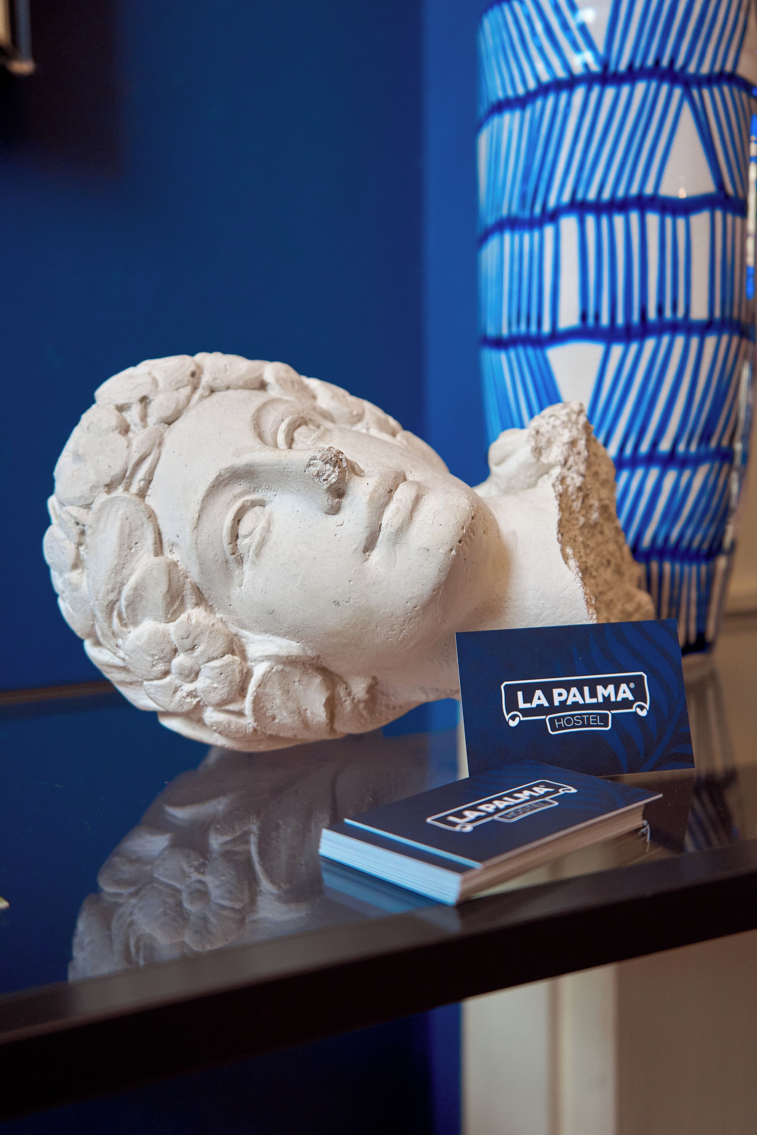 Uma escultura em busto e um vaso com padrão azul e branco sobre uma superfície refletora.