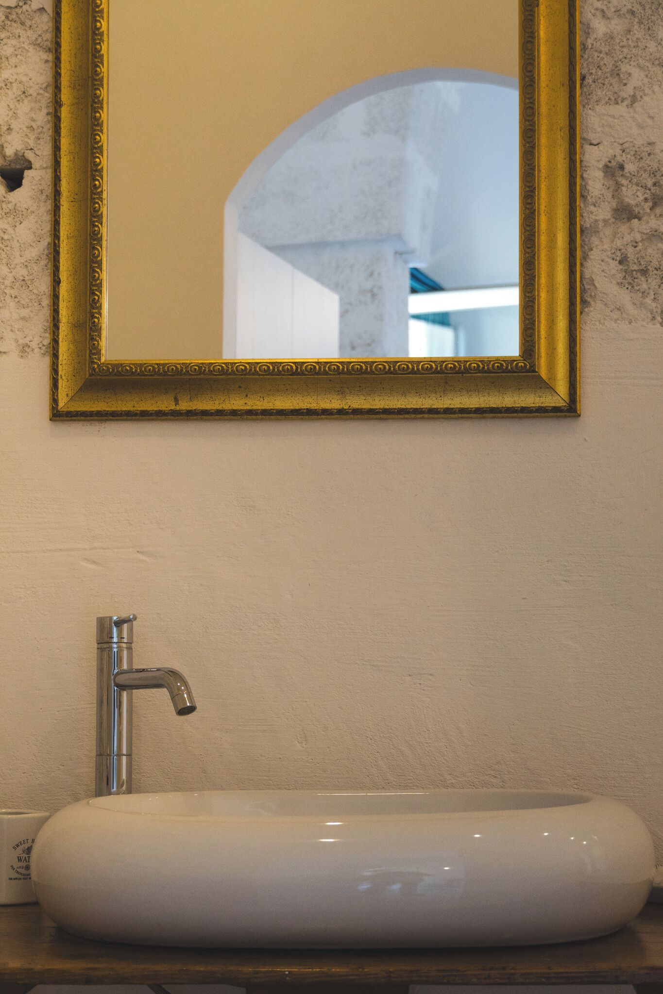 Casa de banho com lavatório branco, espelho com moldura dourada e bica visível.