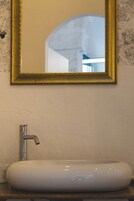 Casa de banho com lavatório branco, espelho com moldura dourada e bica visível.