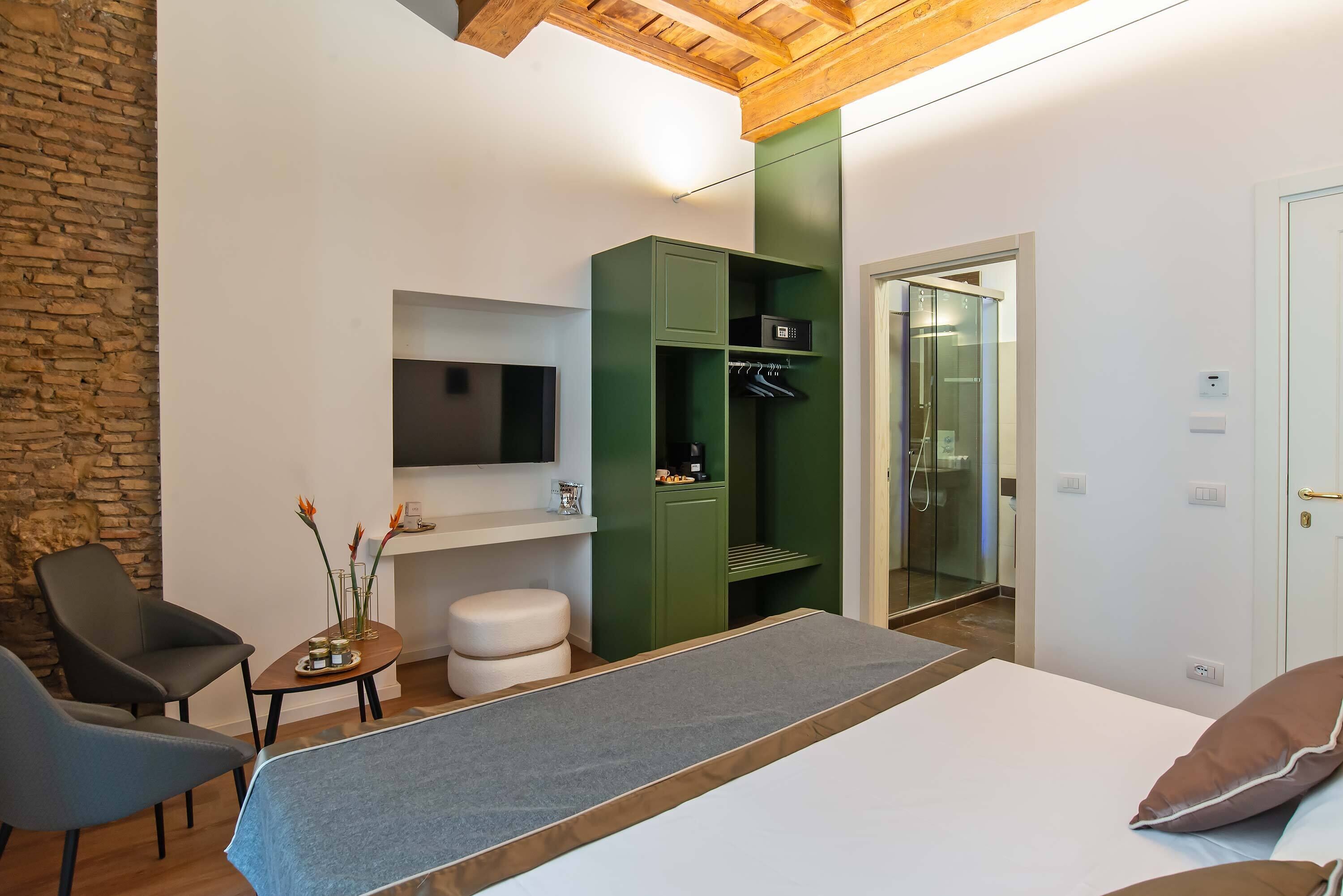 Quarto de hotel moderno com cama, área de estar, TV, guarda-roupa verde e chuveiro.